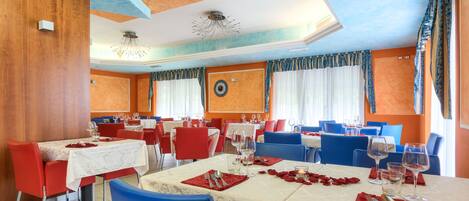 Restaurante com várias mesas, cadeiras vermelhas e azuis e um teto com design singular.