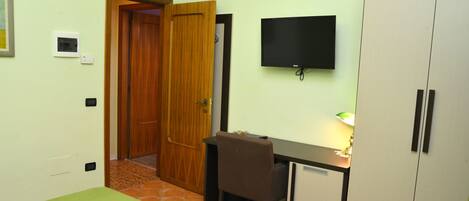 Quarto com cama, escrivaninha, cadeira, televisão e guarda-roupa.