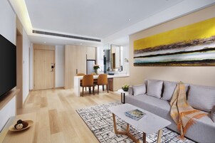 Uma sala de estar moderna com sofá, mesa de centro e televisão. Há uma área de jantar com cadeiras e uma mesa.