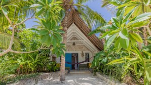 Uma cabana com telhado de palha e porta azul, rodeada por vegetação tropical exuberante.