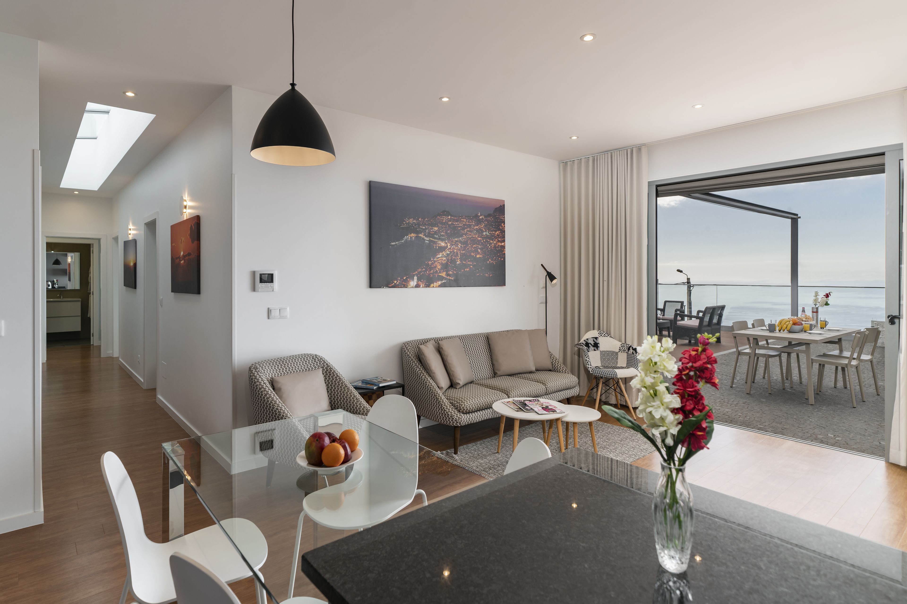 Uma sala de estar moderna com uma mesa de jantar de vidro, um sofá e uma janela grande com vista para a cidade.