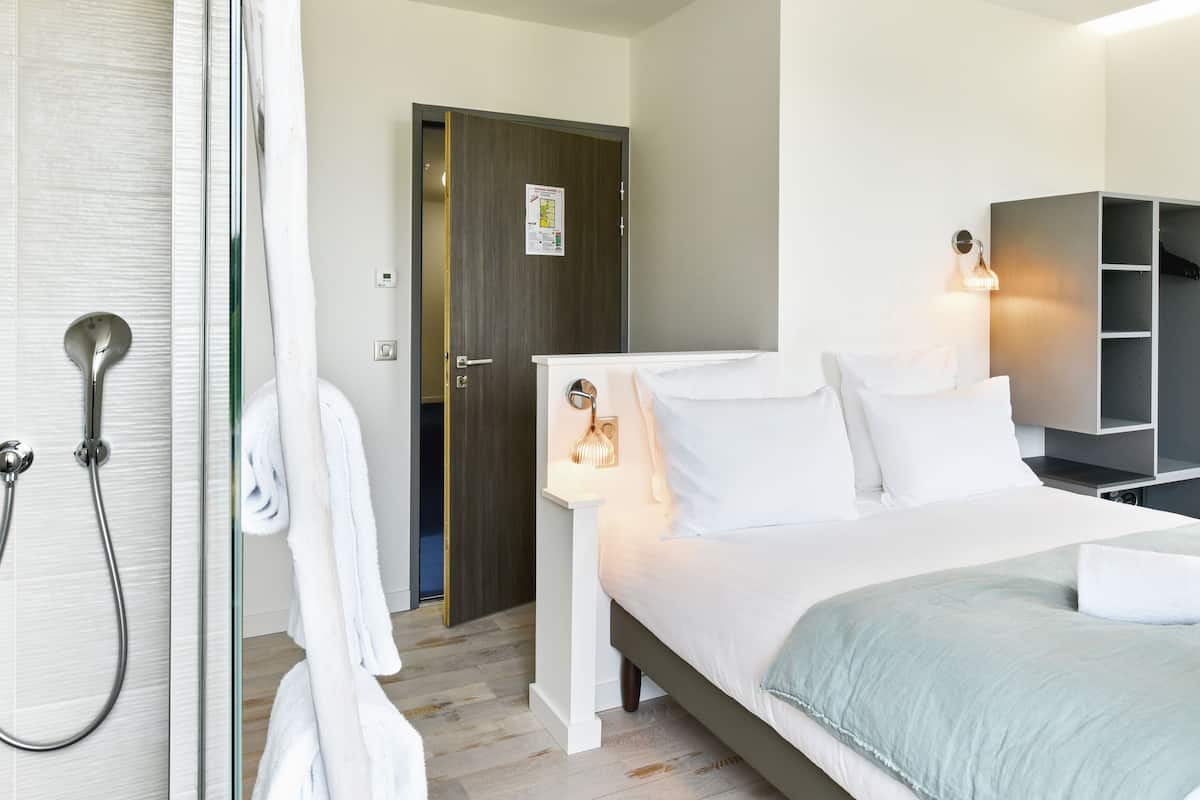Quarto de hotel com cama, chuveiro, roupão e armário.