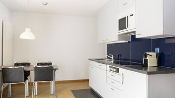 Cozinha moderna com armários brancos, bancada preta e micro-ondas. Duas cadeiras estão dispostas em torno de uma mesa, e uma luminária pendente ilumina o teto.