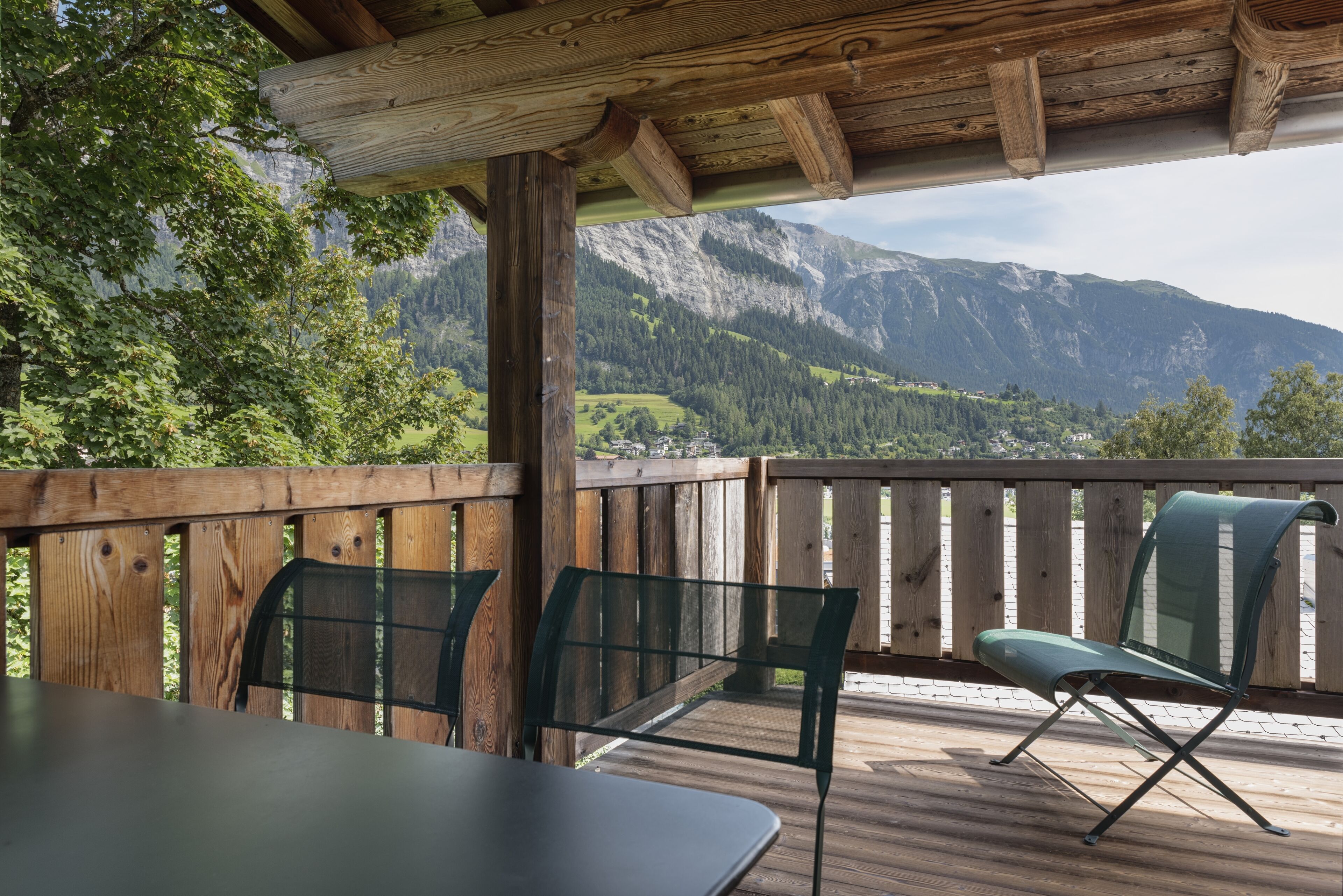 Um deck de madeira com mesa e cadeiras, com vista para uma paisagem montanhosa.