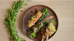Um prato de comida com vegetais, carne e um ramo de ervas.