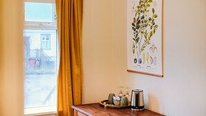 Quarto com janela, uma ilustração botânica emoldurada e uma mesa com uma bandeja de objetos.