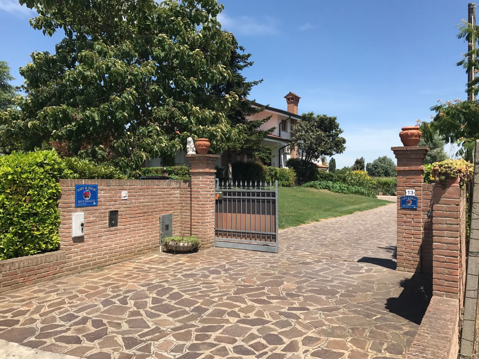 Uma entrada com portão e um caminho de paralelepípedos de pedra que leva a um edifício com fachada de tijolos e chaminé.