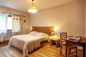 Quarto com cabeceira de madeira, cama com manta branca, mesa de cabeceira com abajur e cadeira com revista.