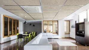 Um escritório moderno com um sofá branco comprido, cadeiras verde-claras e uma mesa branca. Apresenta uma parede com padrão e uma janela grande.