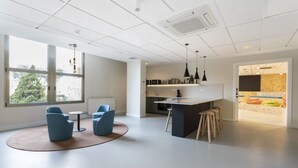 Uma cozinha moderna com bancada, grandes janelas e um espaço de estar com cadeiras azuis.