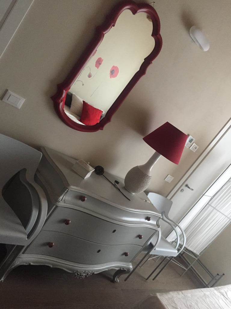 Um quarto com um espelho grande, uma cômoda, um abajur vermelho e uma janela com persianas.