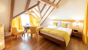 Quarto com teto de madeira, cama com cobertor amarelo, mesa de cabeceira com abajur e uma cadeira.