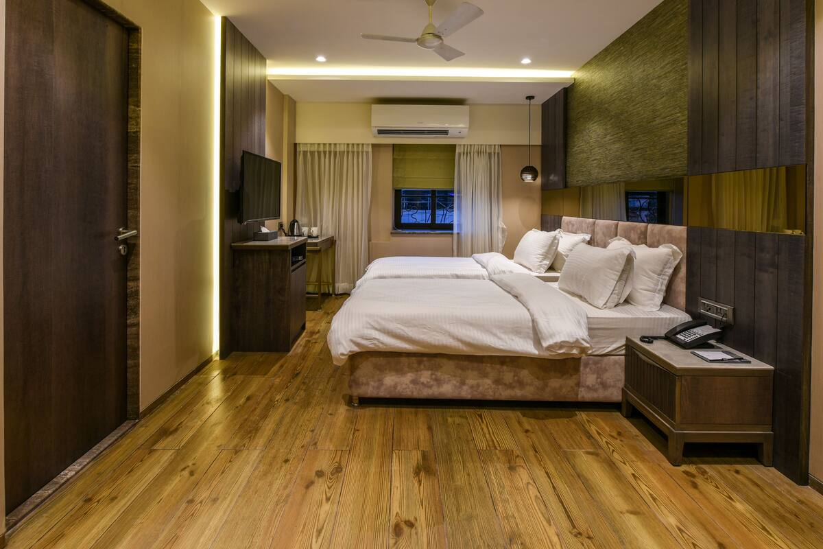 Quarto de hotel moderno com uma cama grande, uma escrivaninha com computador, televisão e ar condicionado.