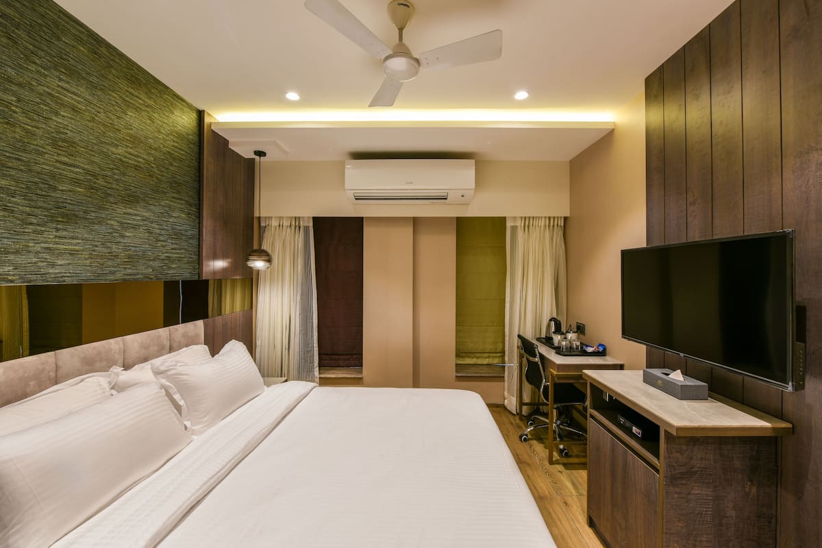 Quarto de hotel com uma cama grande, uma televisão de tela plana, uma escrivaninha com cadeira e um ar condicionado.