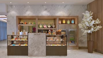 Vitrine de padaria com diversos doces e sobremesas, área refrigerada com bebidas e um arranjo de flores.