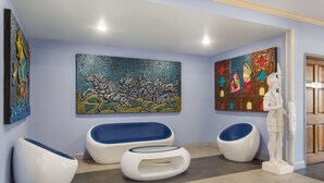 Um lobby moderno com esquema de cores azul e branco, apresentando um mural grande, uma estátua e arranjos de assentos exclusivos.