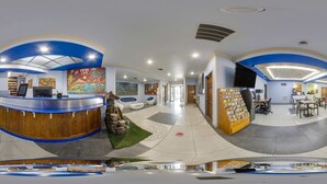 Uma área de recepção moderna com balcão de madeira, um mural e um espaço de estar com mesas e cadeiras.