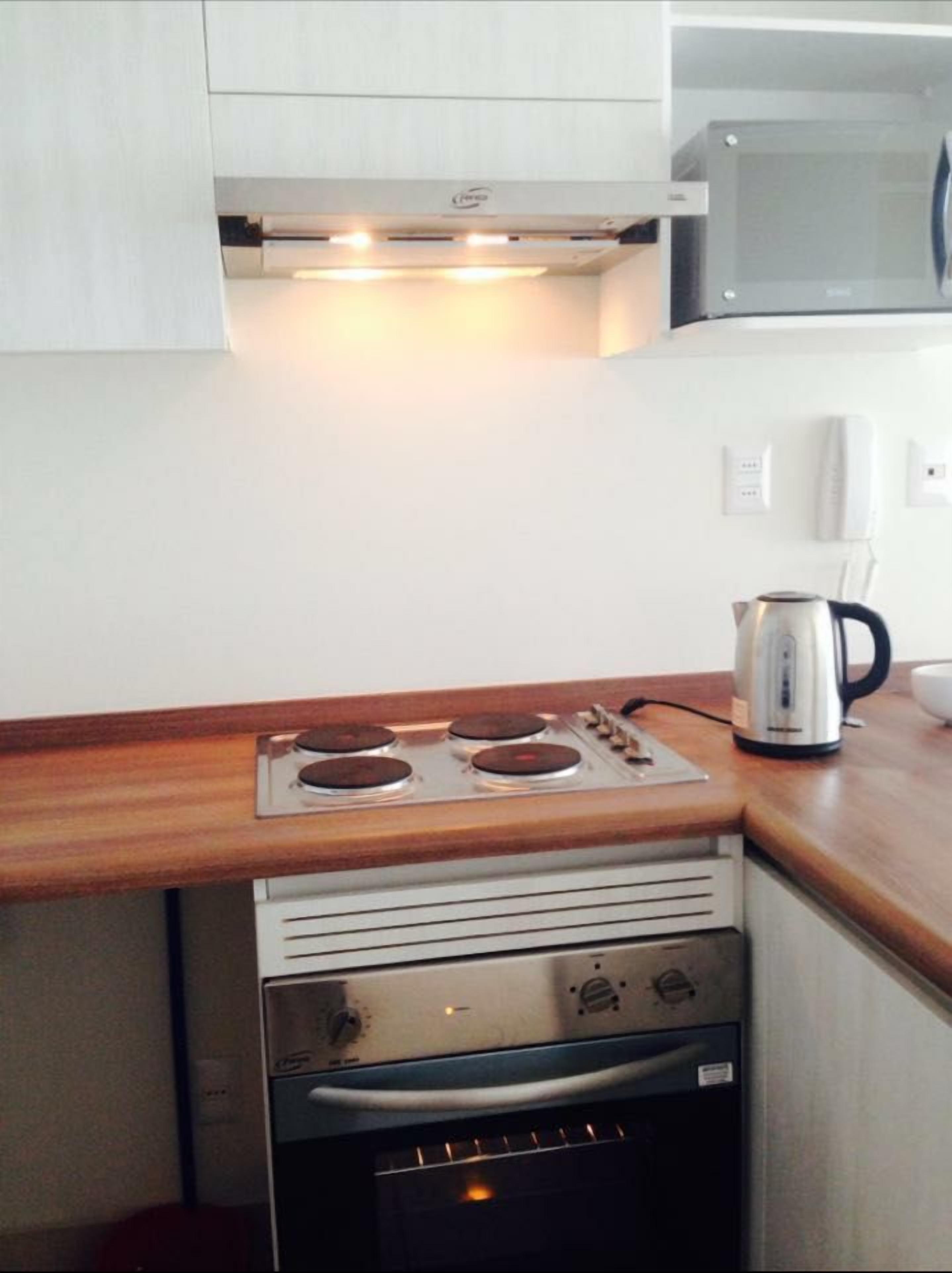 Cozinha compacta com fogão a gás, forno e micro-ondas em cima.