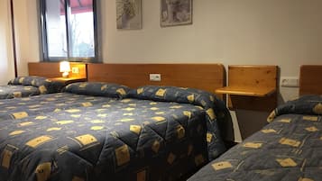 Quarto com duas camas, cada uma com edredom azul e amarelo estampado. Tem cabeceira de madeira, mesa de cabeceira com luminária e janela com persianas.