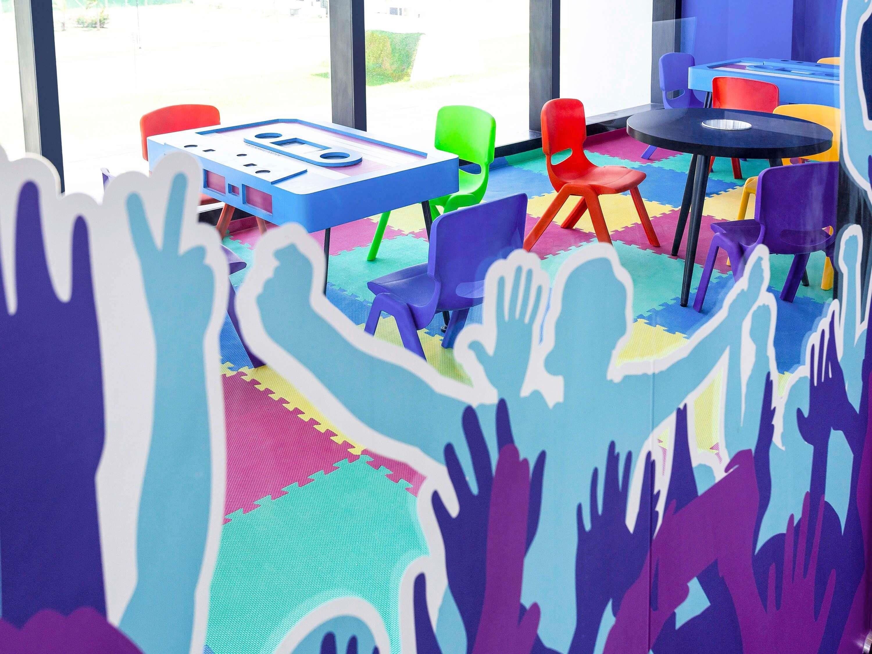 Espaço infantil com mesas e cadeiras coloridas, e uma janela grande que oferece luz natural.