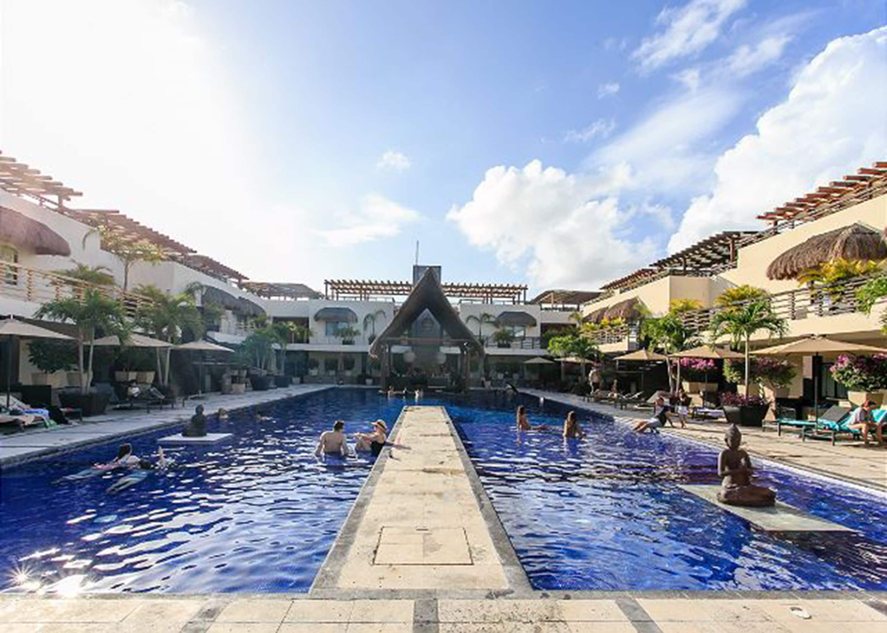 Uma piscina grande ao ar livre com várias pistas, rodeada por edifícios com arquitetura tropical e palmeiras.