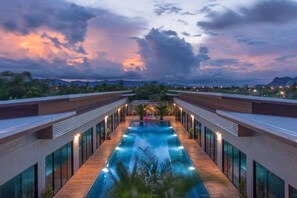 Um hotel moderno com piscina central, cercado por paredes de vidro e passarelas de madeira.