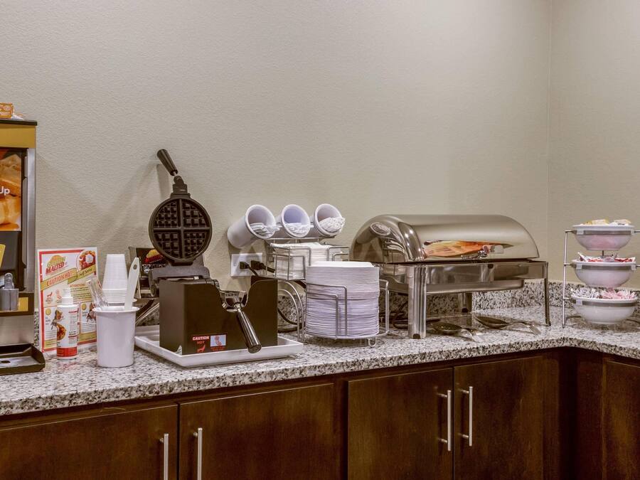 Um balcão de café da manhã com máquina de waffles, cafeteira e pratos empilhados.