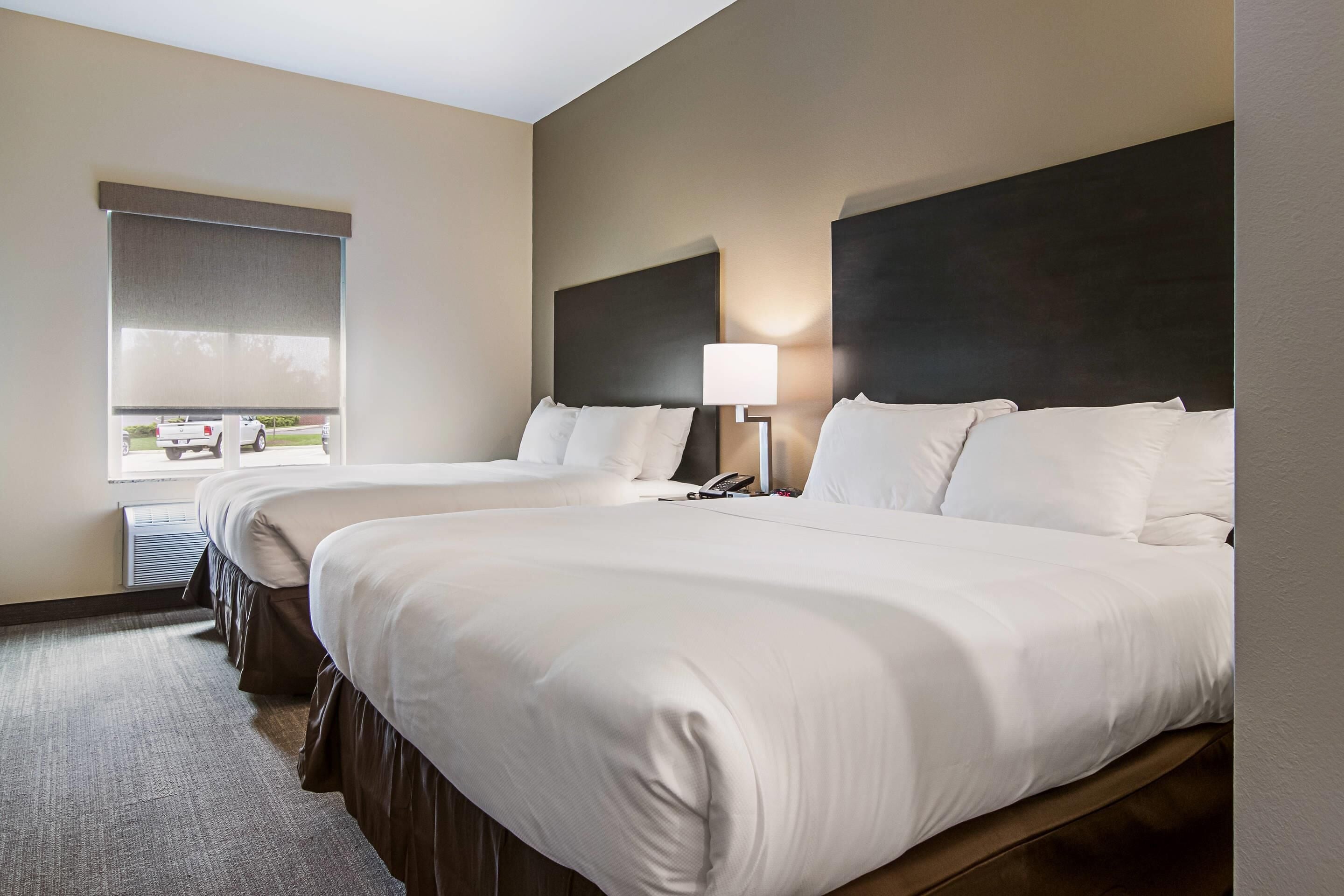 Quarto de hotel com duas camas, uma janela grande e vista para um veículo estacionado lá fora.