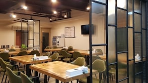 Uma sala de conferências com várias mesas e cadeiras, um quadro branco e uma televisão na parede.