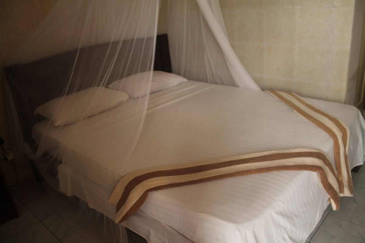 Uma cama com dossel, roupa de cama branca e detalhes em castanho.