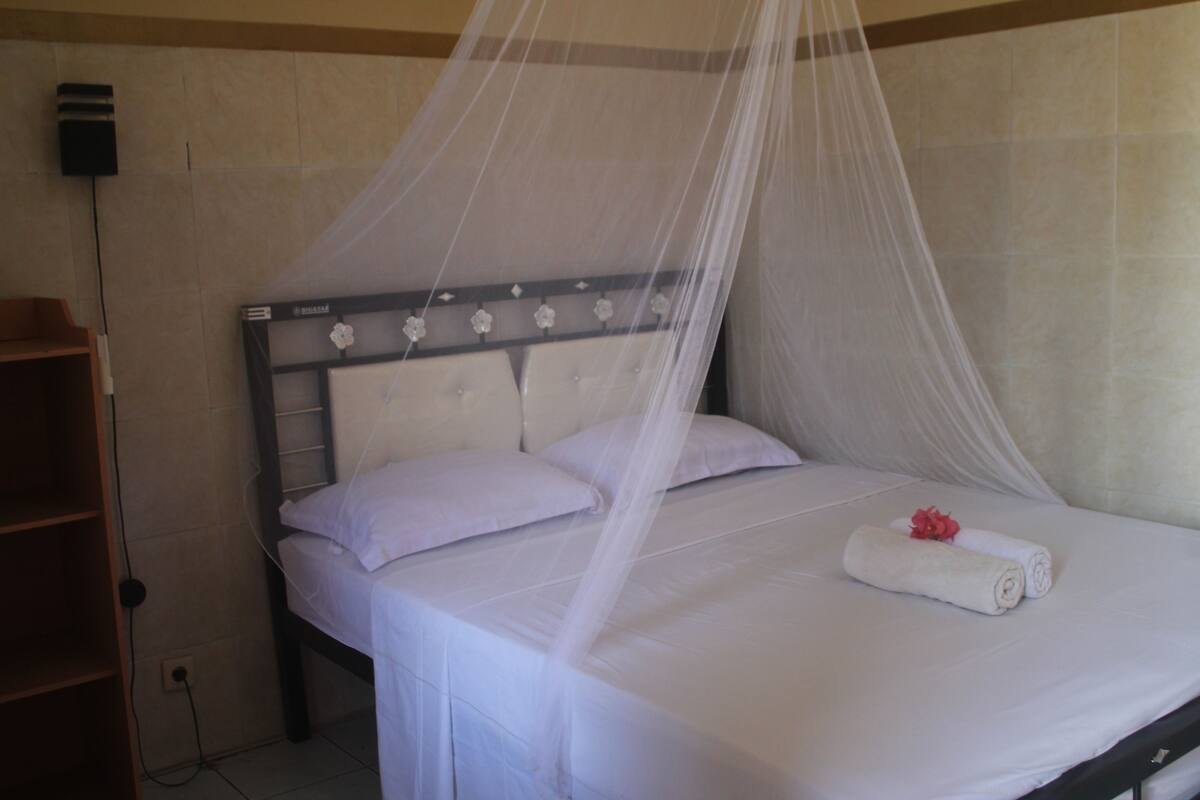 Cama bem arrumada com dossel, lençóis brancos e toalha enrolada com uma flor.