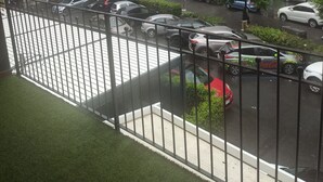 Vista de uma varanda com vista para um estacionamento com vários carros e edifícios ao fundo.