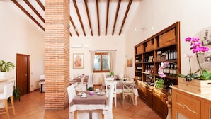 Uma área de refeições com mesas preparadas para dois, um pilar de tijolos e um aparador de vinhos com garrafas.