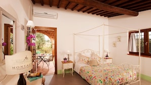 Um quarto com cama de dossel, mesa de cabeceira, mesa auxiliar e uma cadeira. Há uma janela com vista para o verde lá fora.
