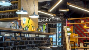 Uma área de bar moderna com banquetas altas, um balcão com copos e um letreiro com a palavra 'HUNGRY'.