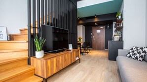 Uma sala de estar moderna com escada de madeira, televisão de tela plana, sofá cinza e um espaço de jantar com mesa e cadeiras.