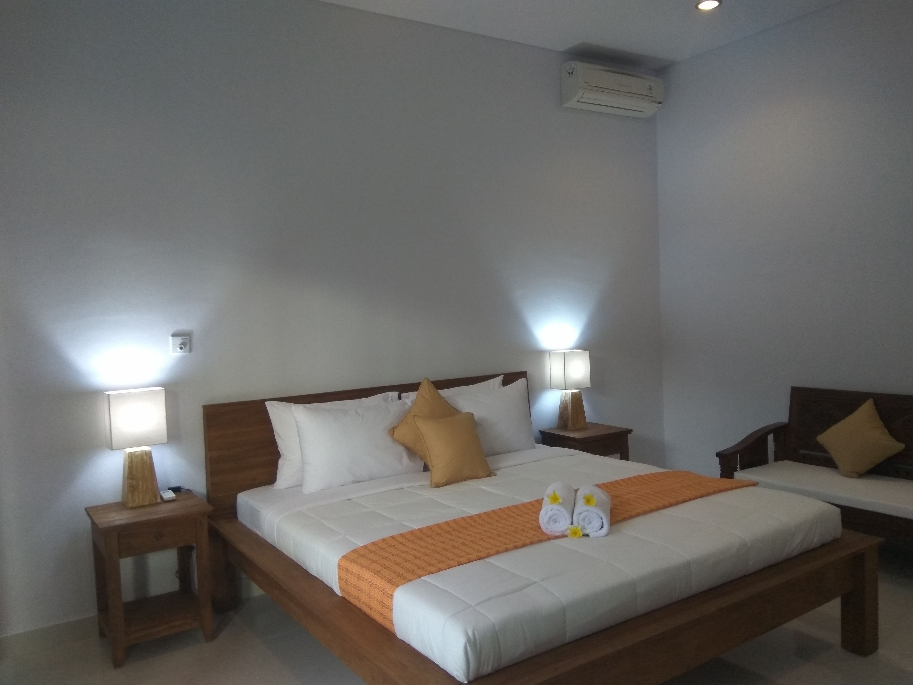Quarto de hotel com uma cama grande, duas mesas de cabeceira com luminárias, um painel de cabeceira de madeira e um aparelho de ar condicionado no teto.