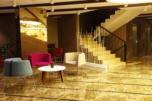 Um hall de entrada com piso de mármore, escada e áreas de estar com cadeiras e uma mesa.