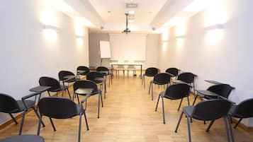 Uma sala de conferências com fileiras de cadeiras voltadas para um quadro branco, um projetor e uma tela.