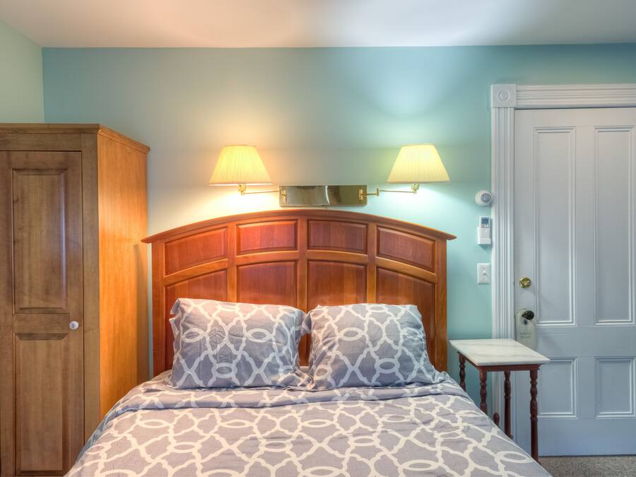 Quarto com cabeceira de madeira, duas luminárias de cabeceira, mesa de apoio e porta com chave de serviço.