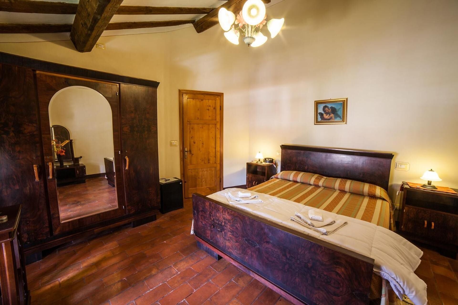 Quarto com cama de madeira, mesa de cabeceira, escrivaninha, cadeira, guarda-roupa e porta.