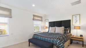 Quarto com cama grande, um banco, duas mesas de cabeceira com luminárias e janela com persianas.