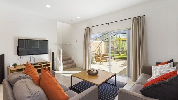 Uma sala de estar moderna com televisão de tela plana, um sofá, uma mesa de centro e uma porta de vidro deslizante que dá para um pátio externo.