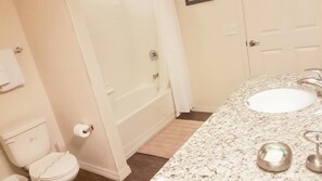 Casa de banho com sanita branca, lavatório com bancada de mármore e zona de duche.