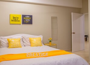 Quarto com cama, duas obras de arte motivacionais na parede, mesa de cabeceira com um vaso de flores e porta que dá para outro cômodo.