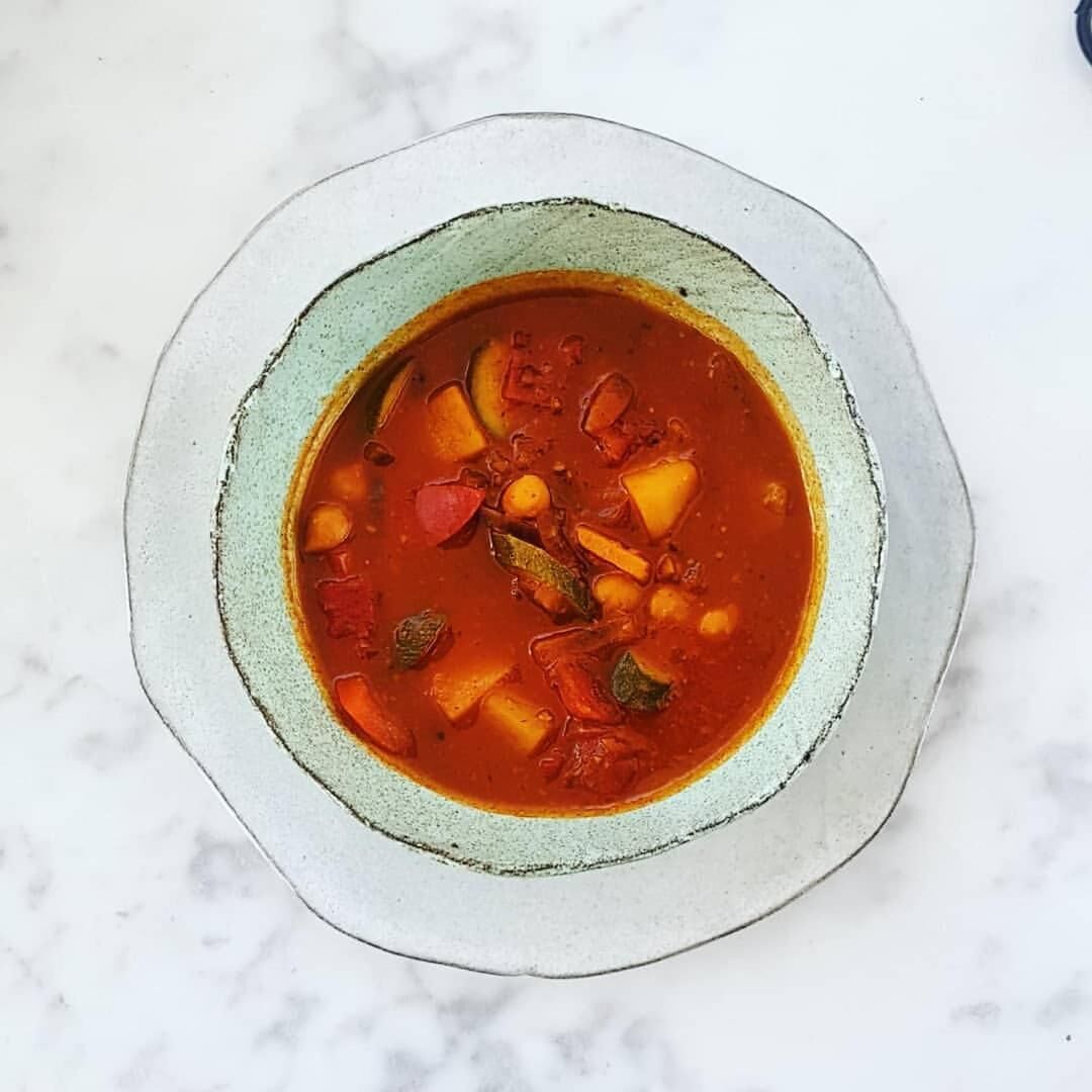 Uma tigela de sopa com vários legumes e caldo transparente, servida em uma tigela de cerâmica sobre uma superfície de mármore.