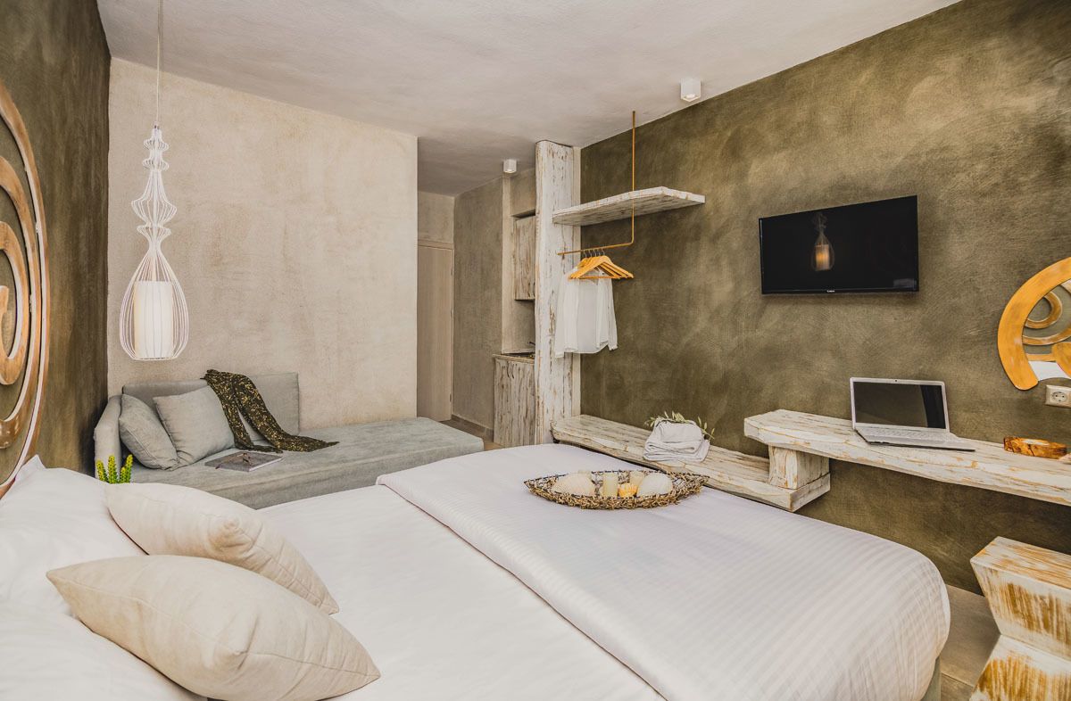 Quarto moderno com uma cama grande, uma TV na parede e um laptop em uma prateleira de madeira.