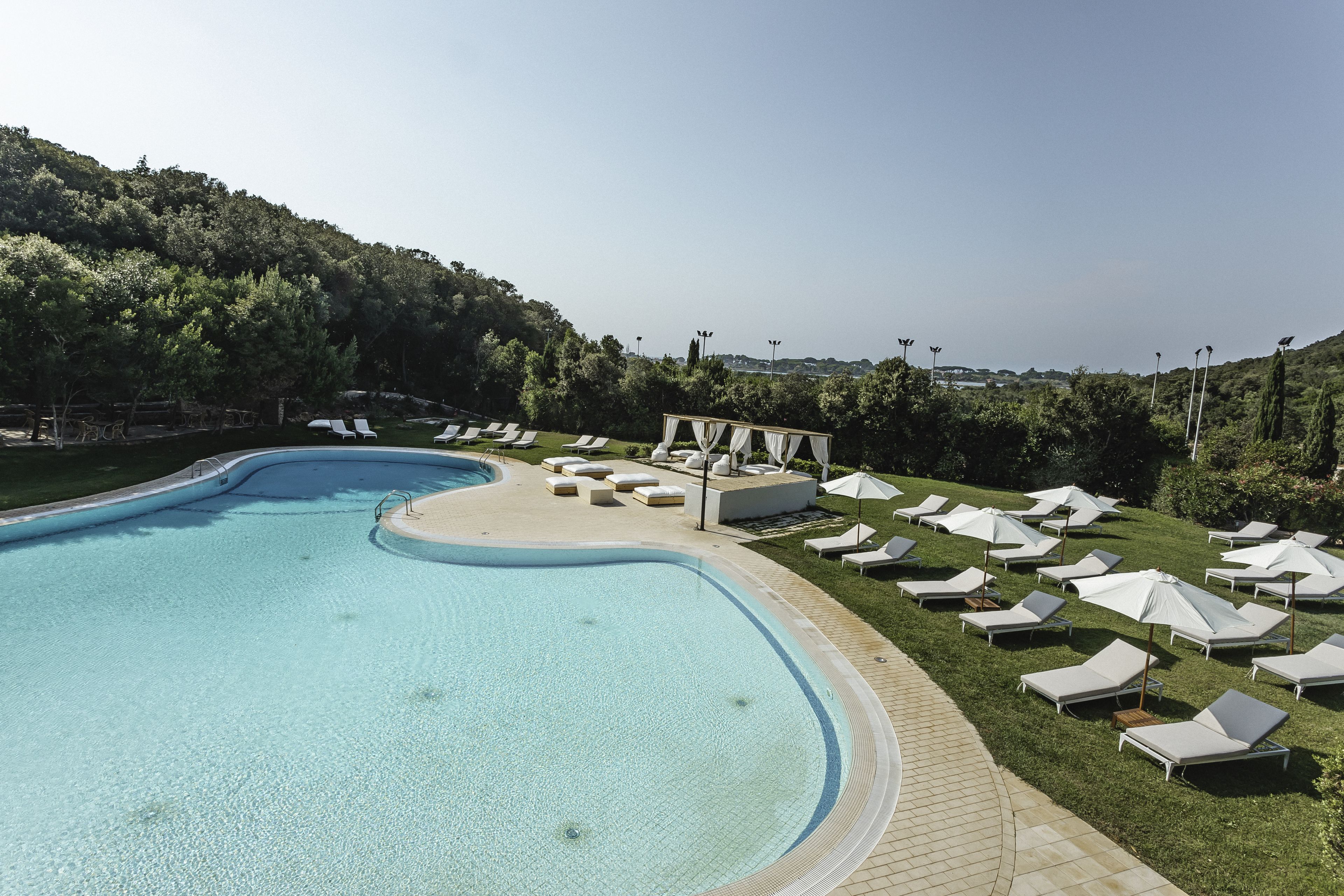 Uma piscina com espreguiçadeiras e guarda-sóis, cercada por vegetação e uma paisagem montanhosa.