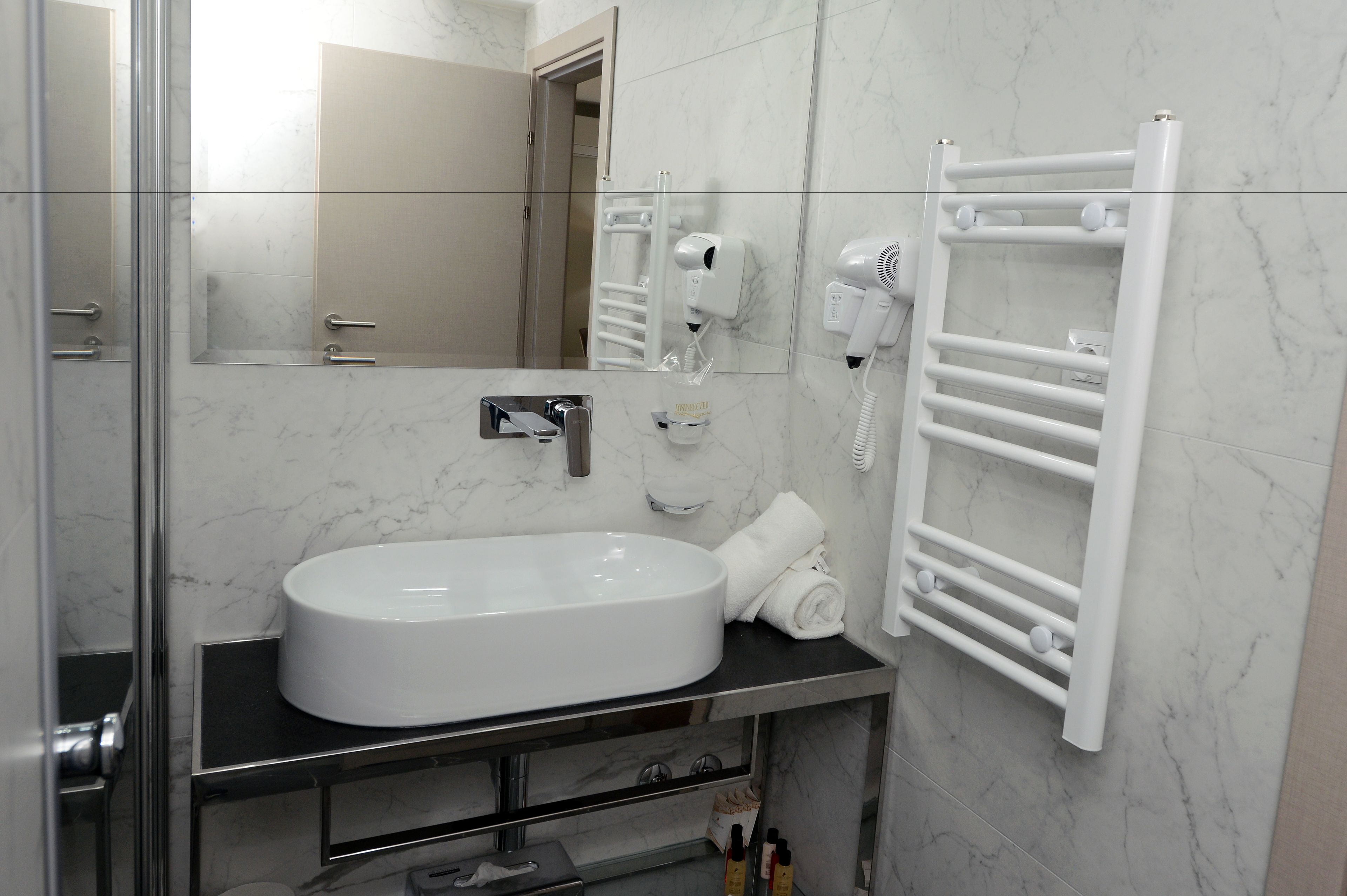 Uma casa de banho moderna com uma pia branca, um espelho, um porta-toalhas e um secador de cabelo.