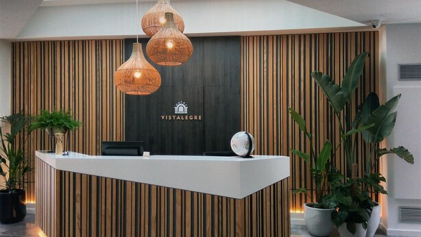 Balcão de recepção de hotel com design moderno, apresentando um painel de madeira ao fundo, três luminárias pendentes e um balcão de atendimento.